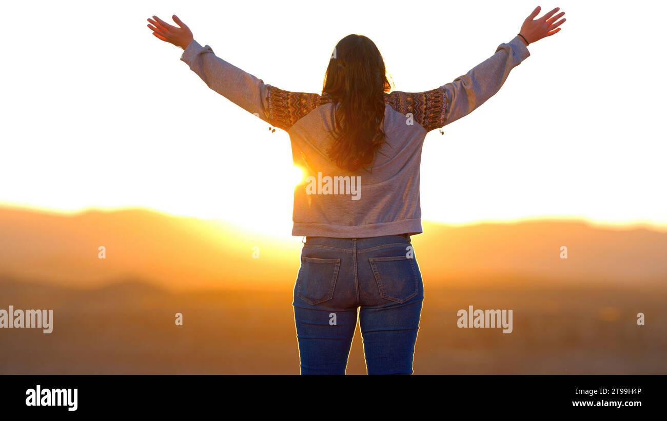 Young woman standing on a cliff at Grand Canyon and raising her arms ...