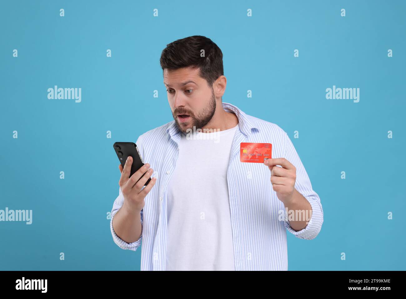 Scared man with credit card and smartphone on light blue background. Be ...