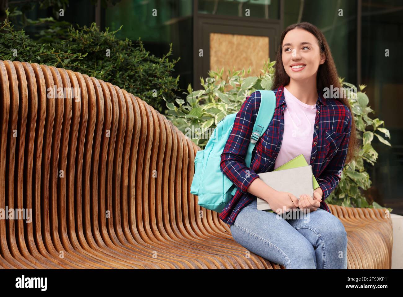 Happy young student with notebooks on bench outdoors, space for text ...