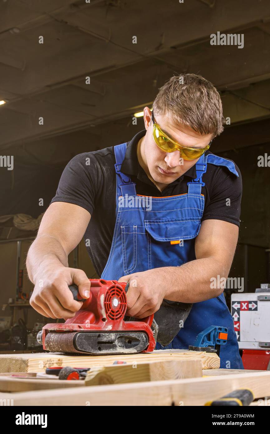Portrait of a young man carpenter using electric sanding machine to ...