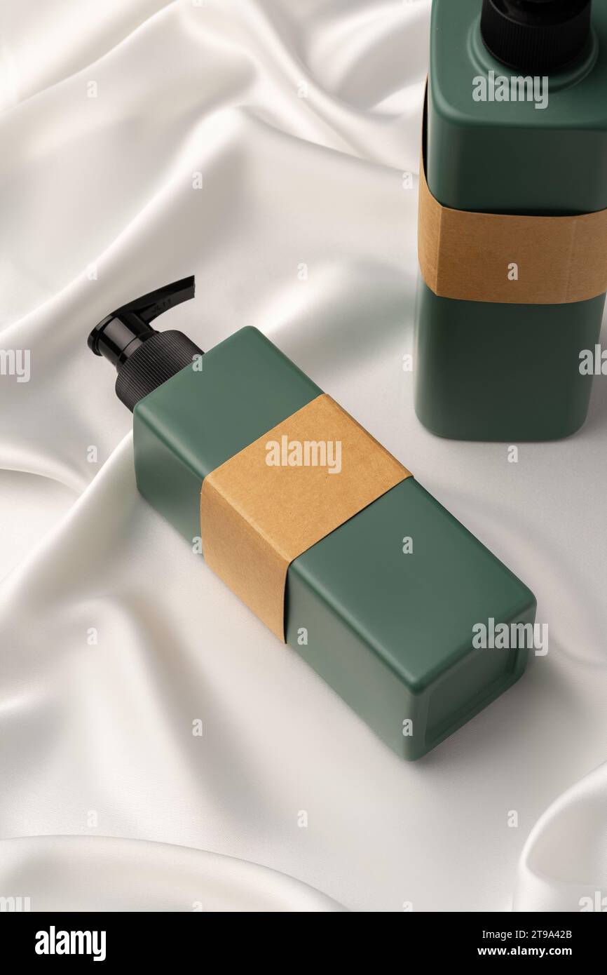 Dark green plastic bottles for skincare products mock up on white silk ...