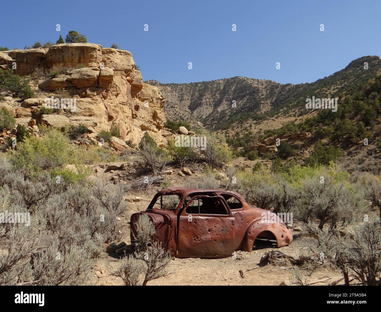 Rusted antique car with bullet holes on a sunny day next to eroded rock ...