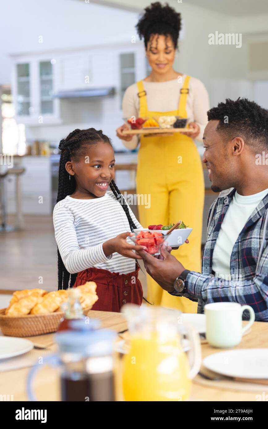 Happy african american family bringing fresh fruits on table in dining room at home, copy space ...