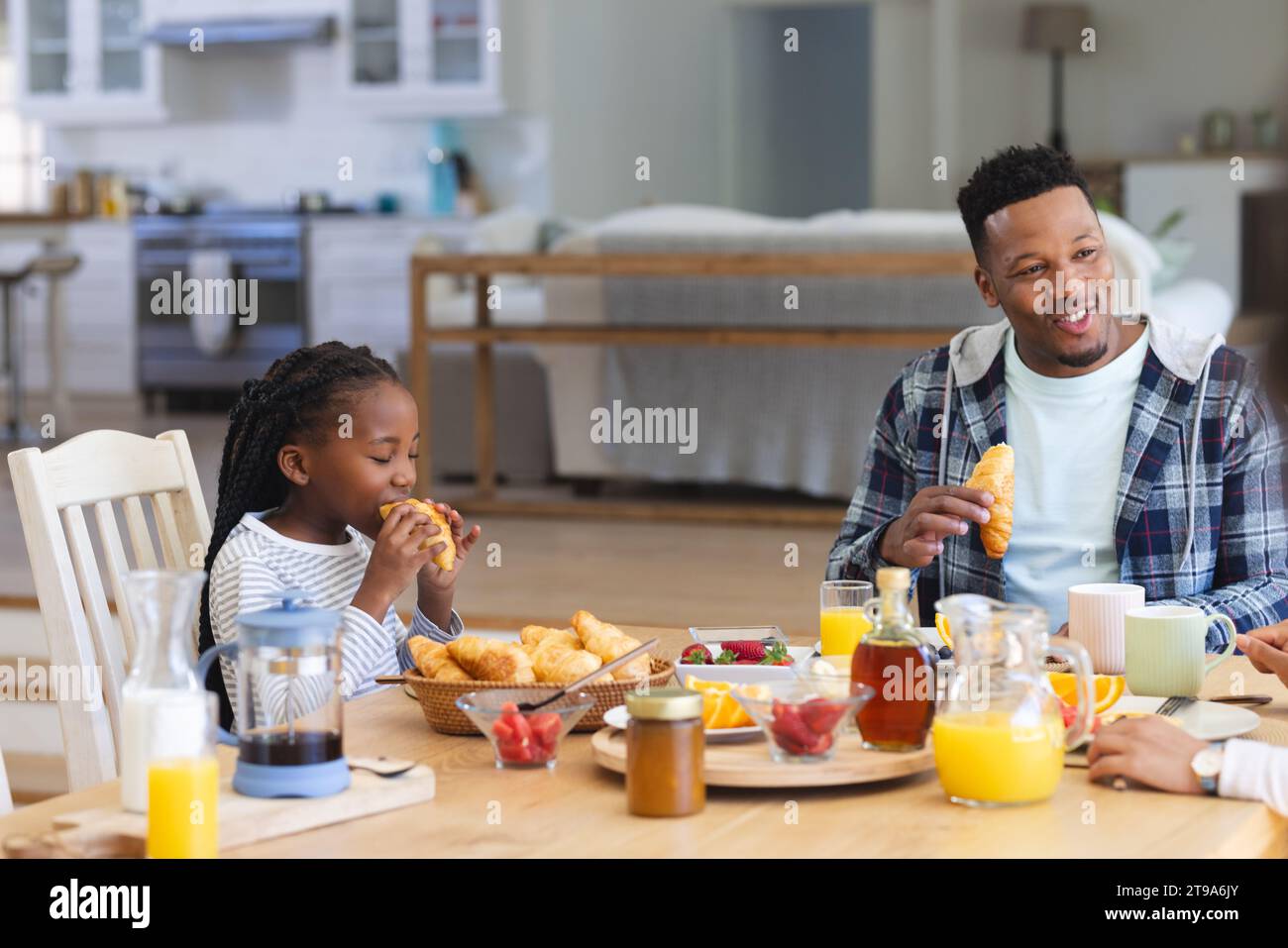 Happy african american girl eating croissant at table at home, copy space. Togetherness ...