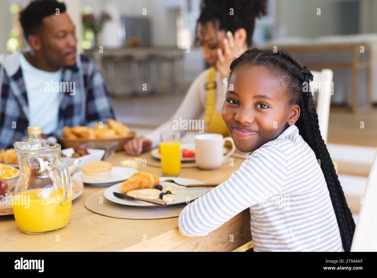 Happy african american girl sitting at table, having a snack with family at home, copy space ...