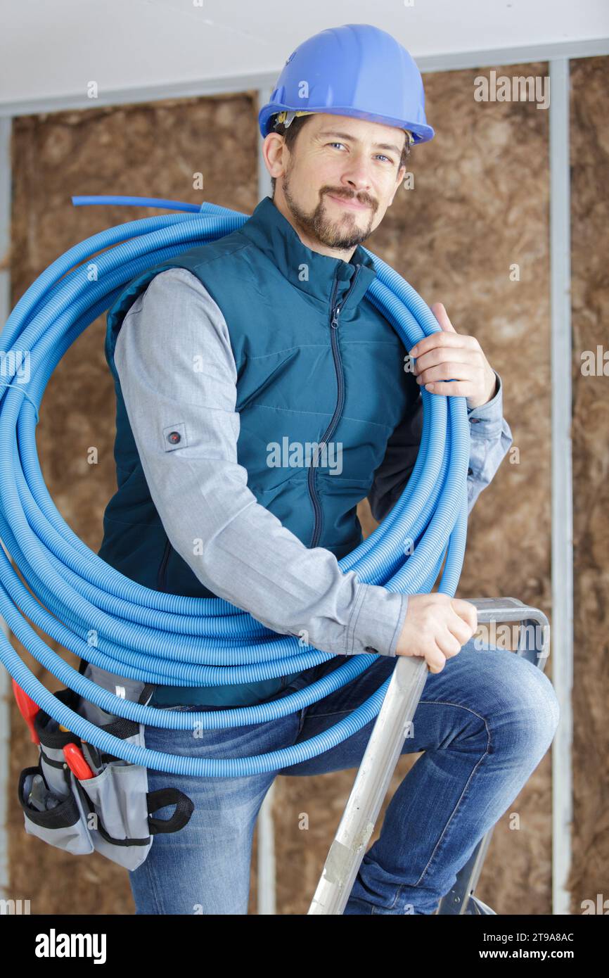 male tradesman with reel of blue pipe on his shoulder Stock Photo - Alamy