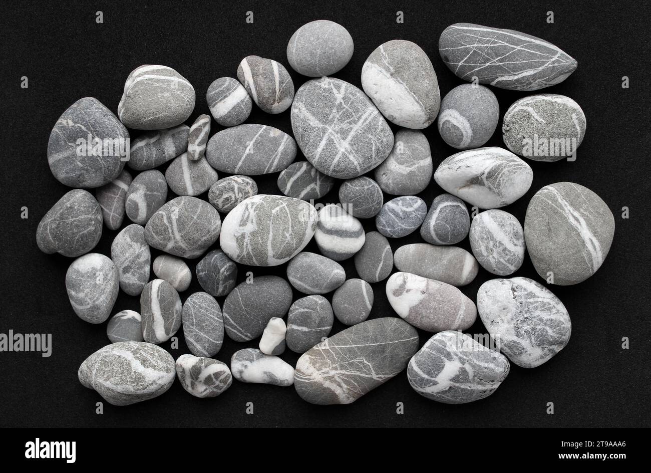 Bunch of smooth gray granite stones with white quartz veins on black ...