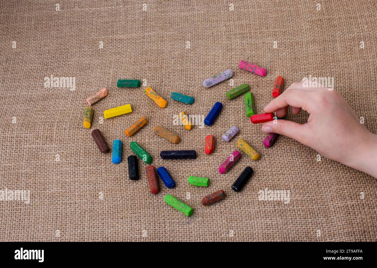 Hand holding a crayon by crayons forming a heart shape Stock Photo - Alamy