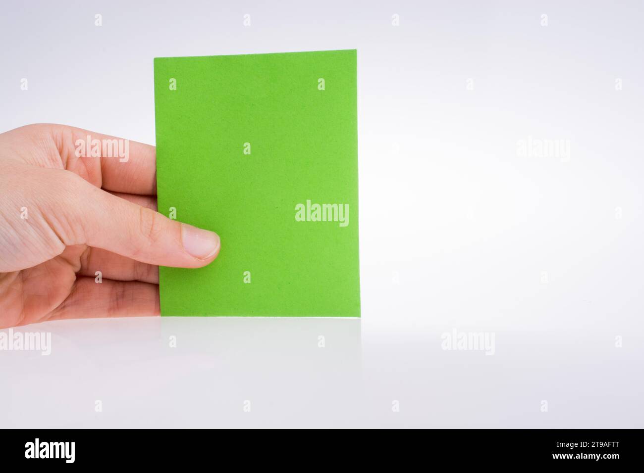 Hand holding a light green color rectangular paper on a white ...
