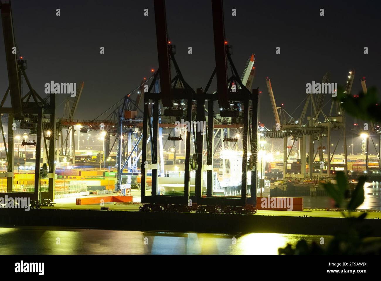 Industrial cranes and containers at a busy harbor at night, illuminated ...
