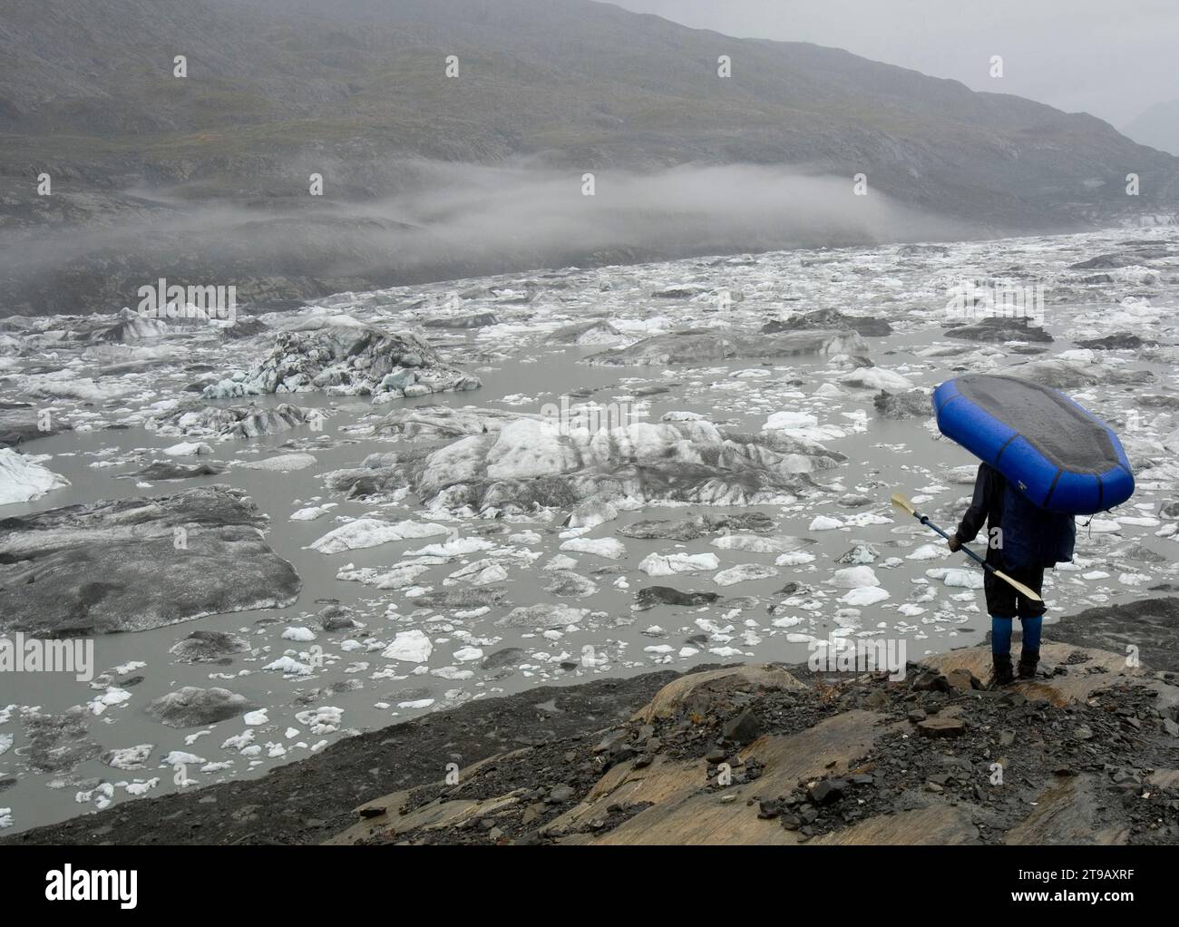 Man looking over an iceberg filled lake with a pack raft on his head ...