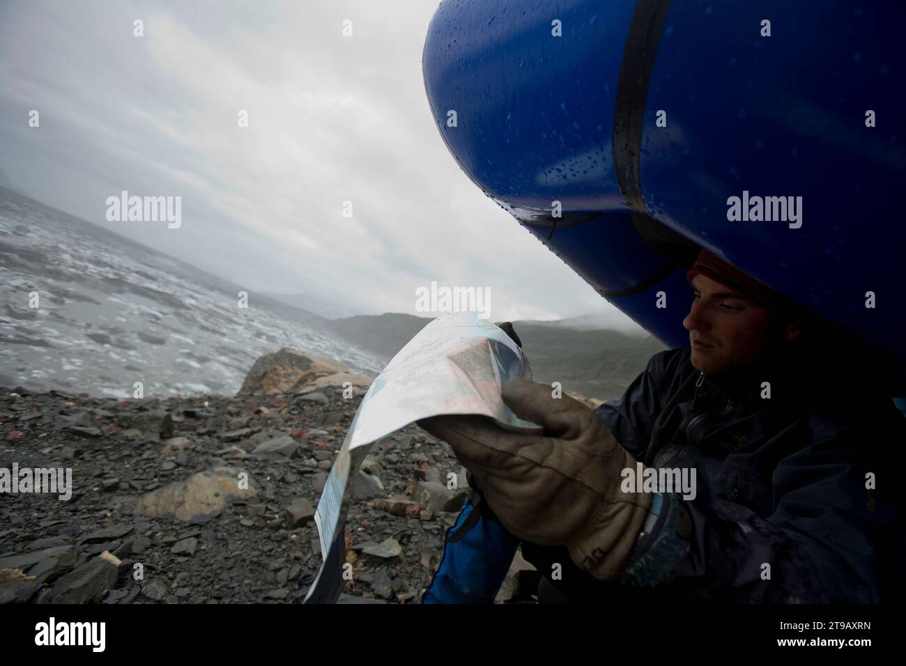 Man sitting under a pack raft next to an iceberg filled lake looking at ...