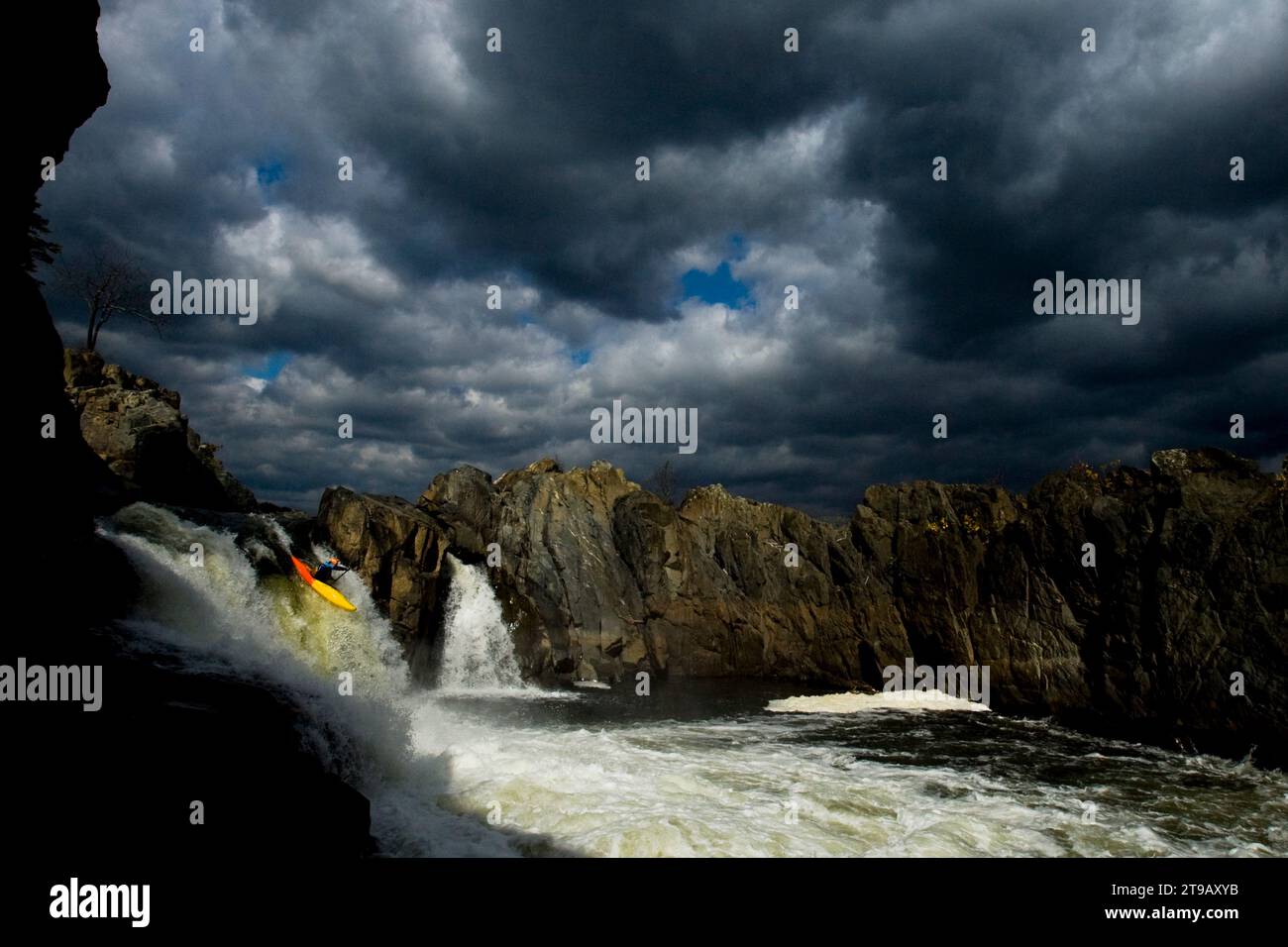 Wide angle of a male kayaker going off of a waterfall with dark ...