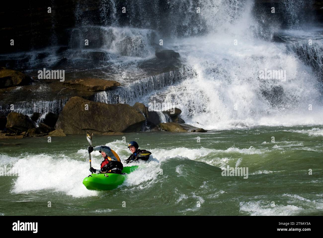 Two male kayakers paddling around waterfalls in a two person kayak ...
