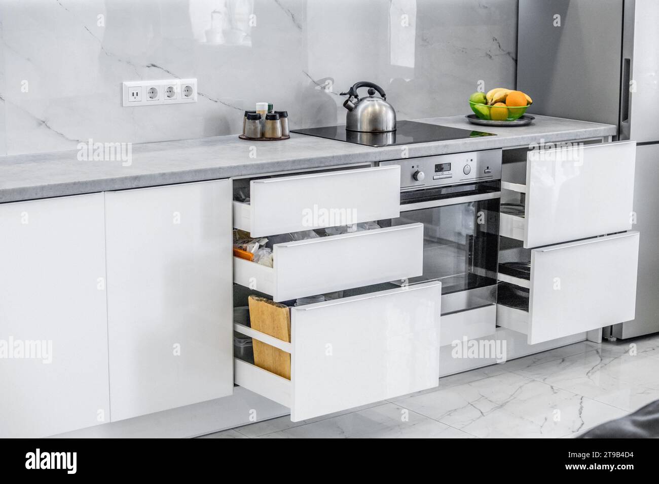 well-organized and modern kitchen featuring white cupboards and marble ...