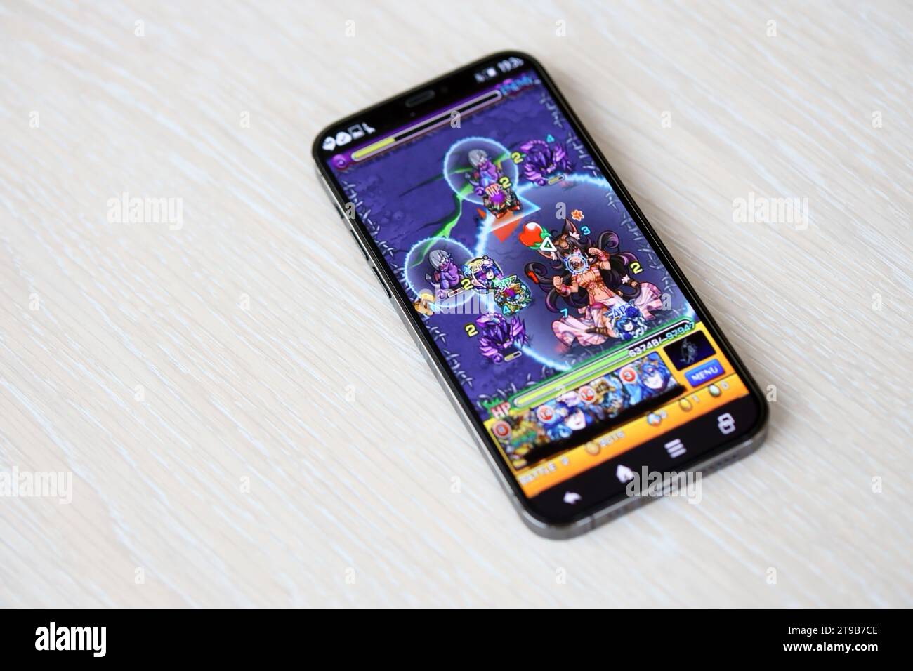 Monster Strike mobile iOS game on iPhone 15 smartphone screen on wooden ...