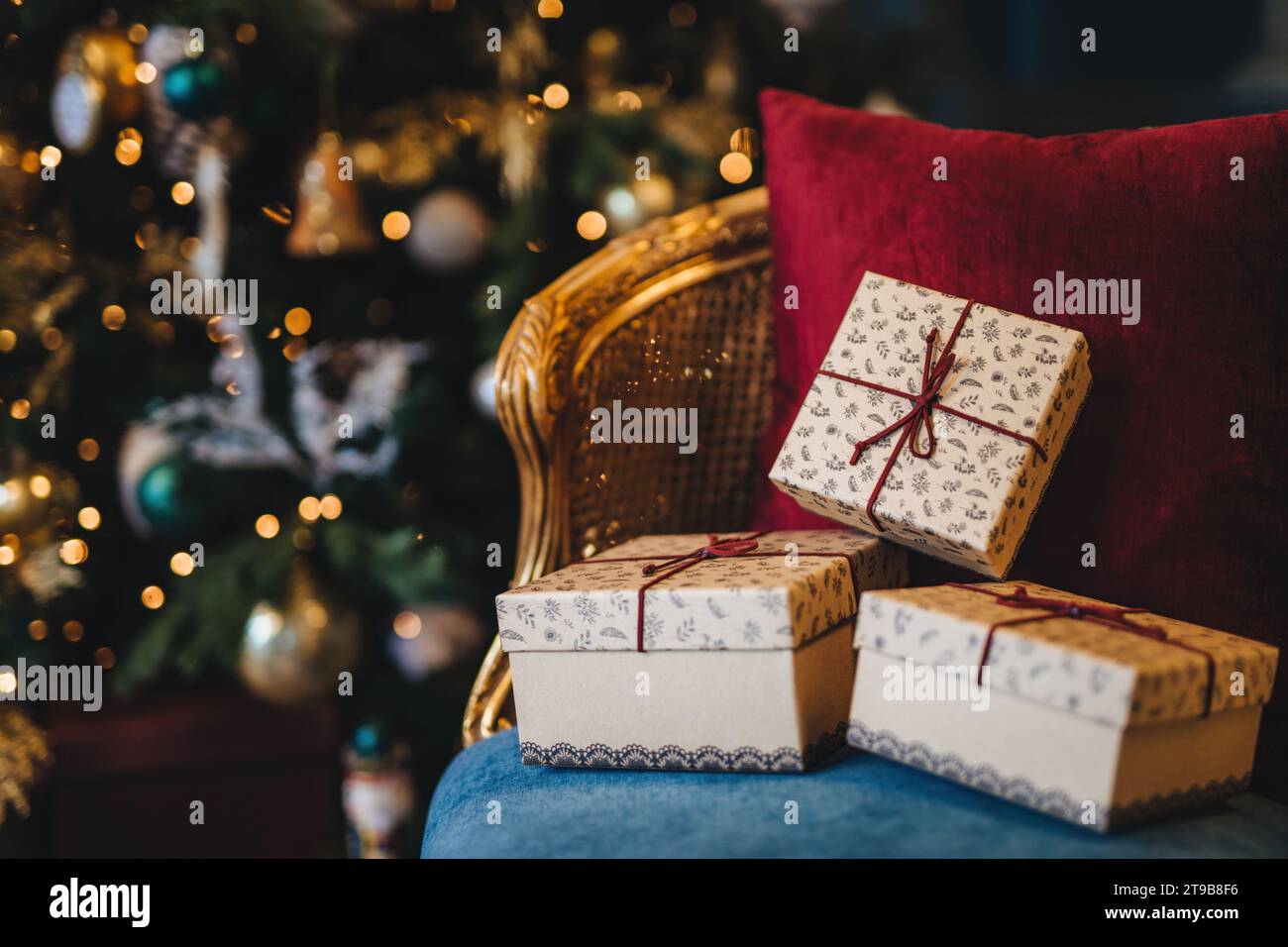Gift boxes with elegant wrapping on a vintage chair, a plush red pillow ...