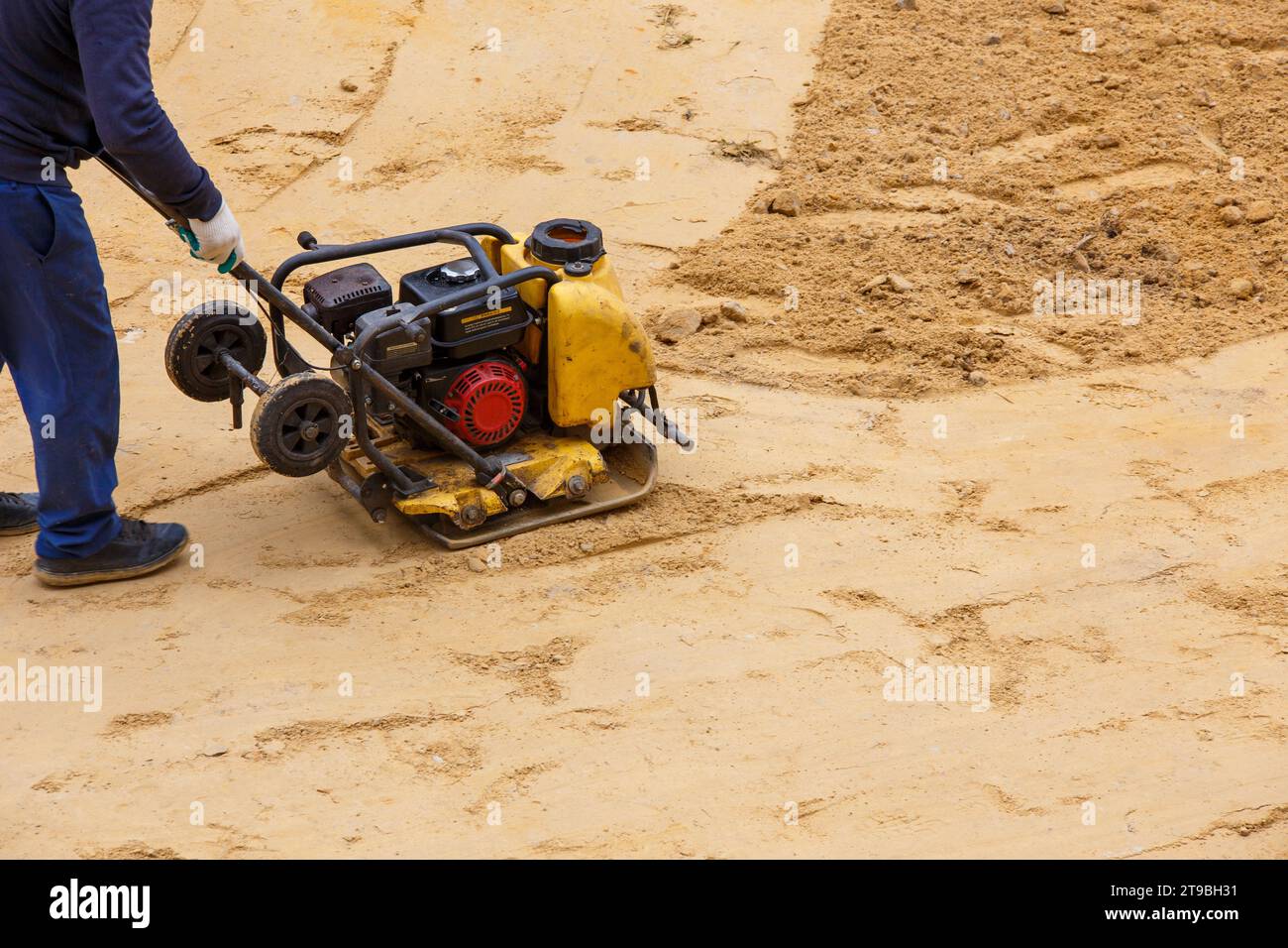 Worker using vibratory plate compactor for compaction sand during path ...