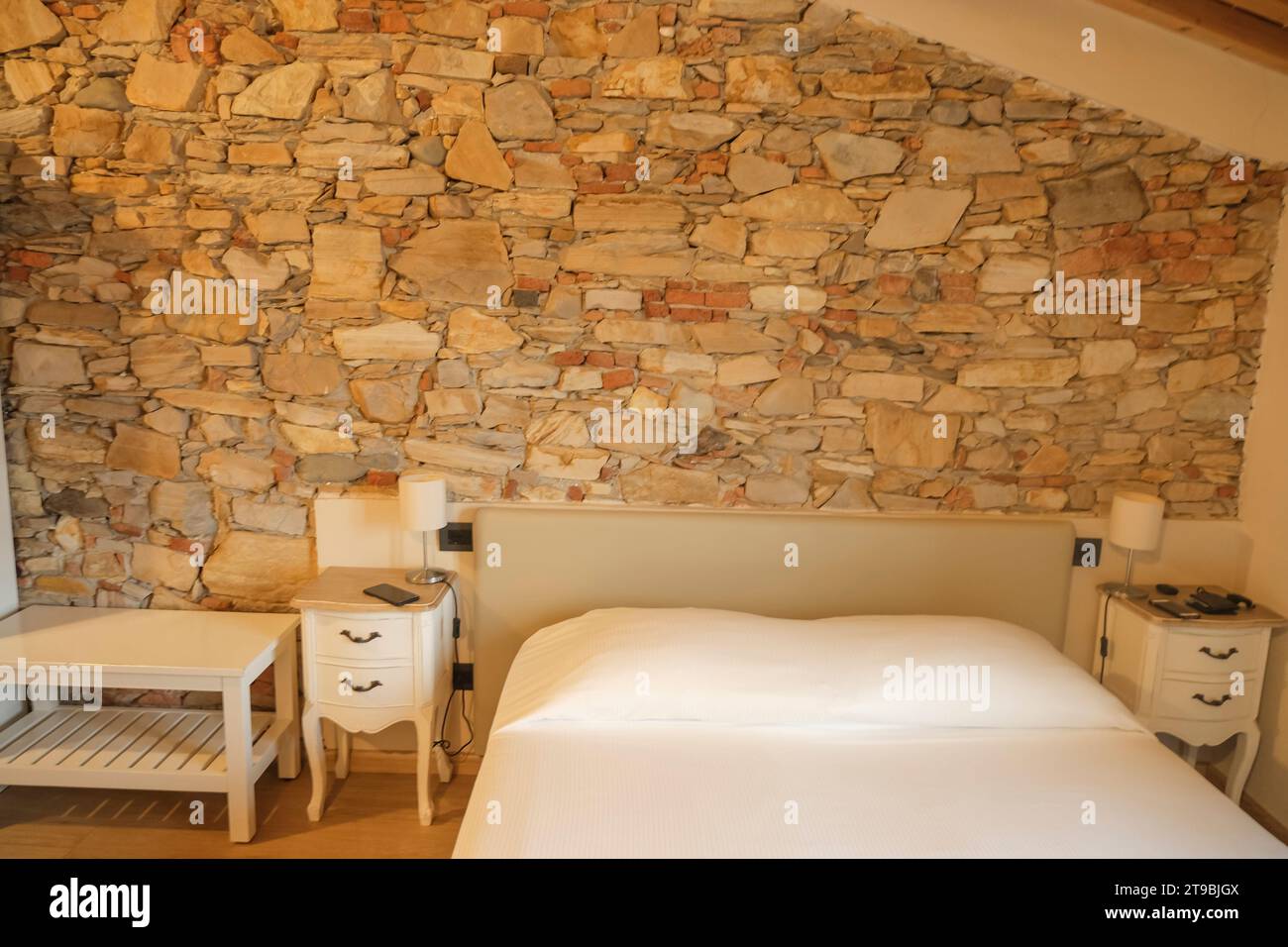interior of a hotel room with a wall made of stones and white furniture ...