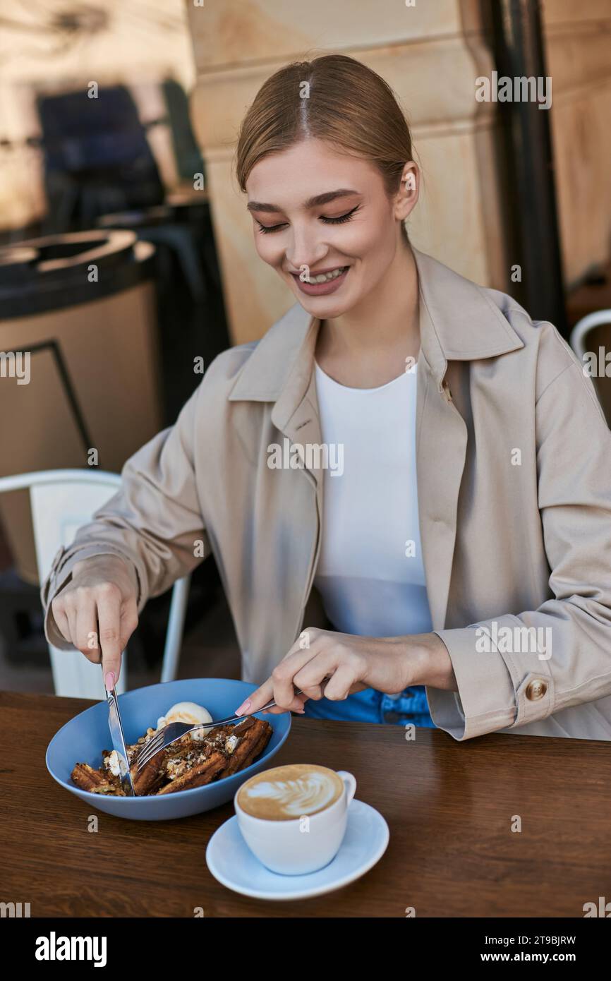 happy young woman in trench coat eating her belgian waffles with ice ...