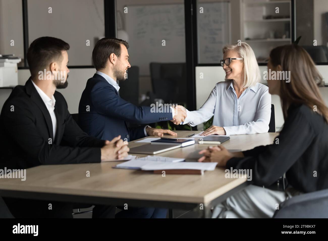 Happy elder businesswoman giving handshake to younger project manager ...