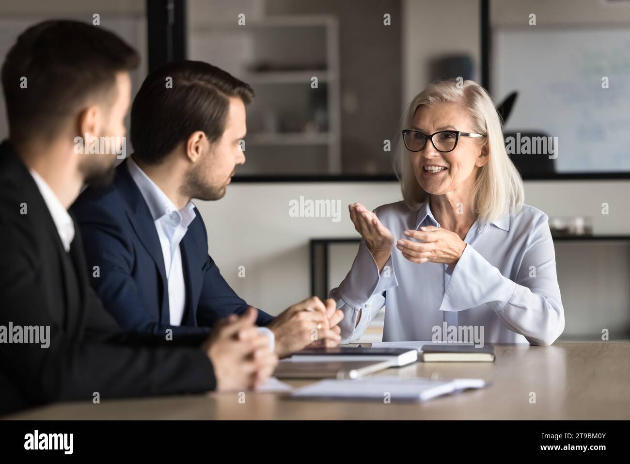 Positive senior boss woman speaking to younger professional men Stock ...