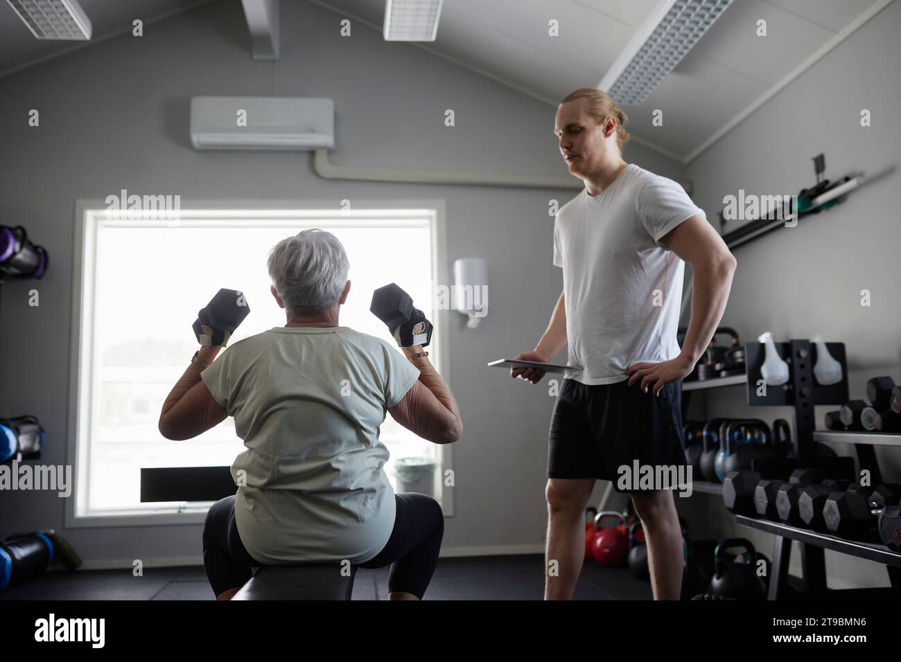 Woman exercising with dumbbell with trainer checking his progress Stock ...