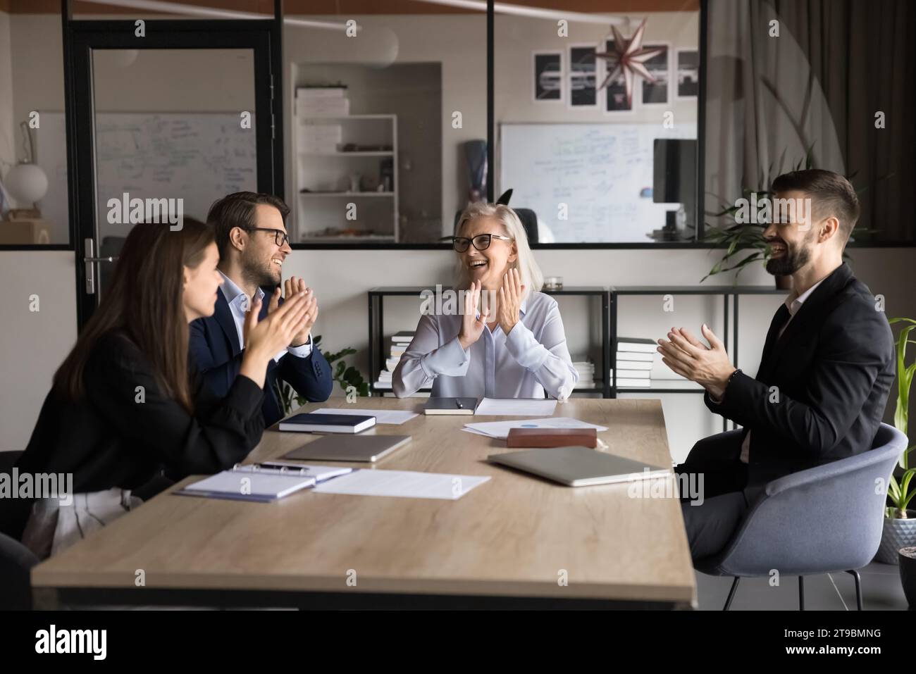 Happy elder and younger business colleagues applauding excited senior ...