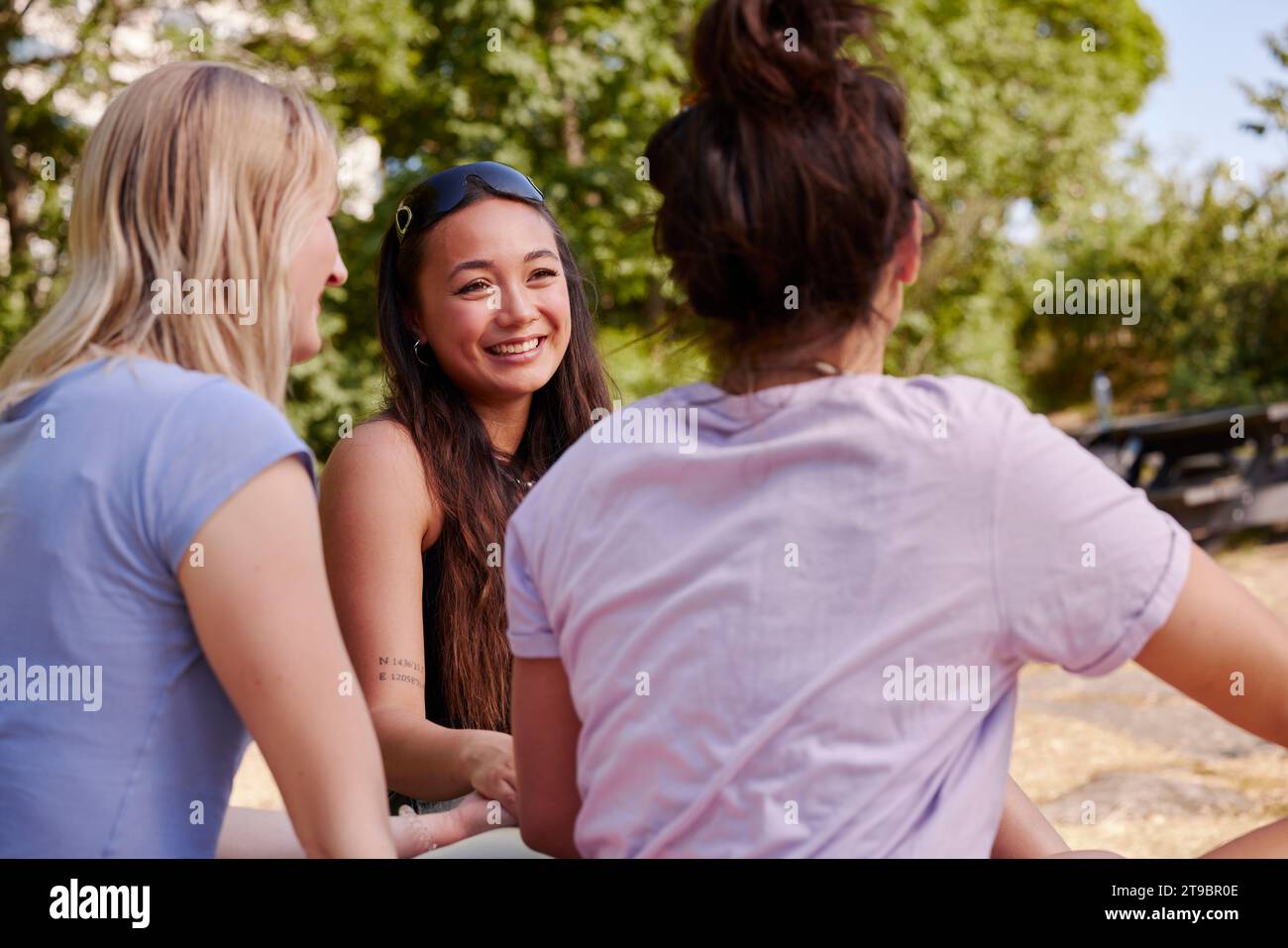 Three young female friends sitting together talking Stock Photo - Alamy