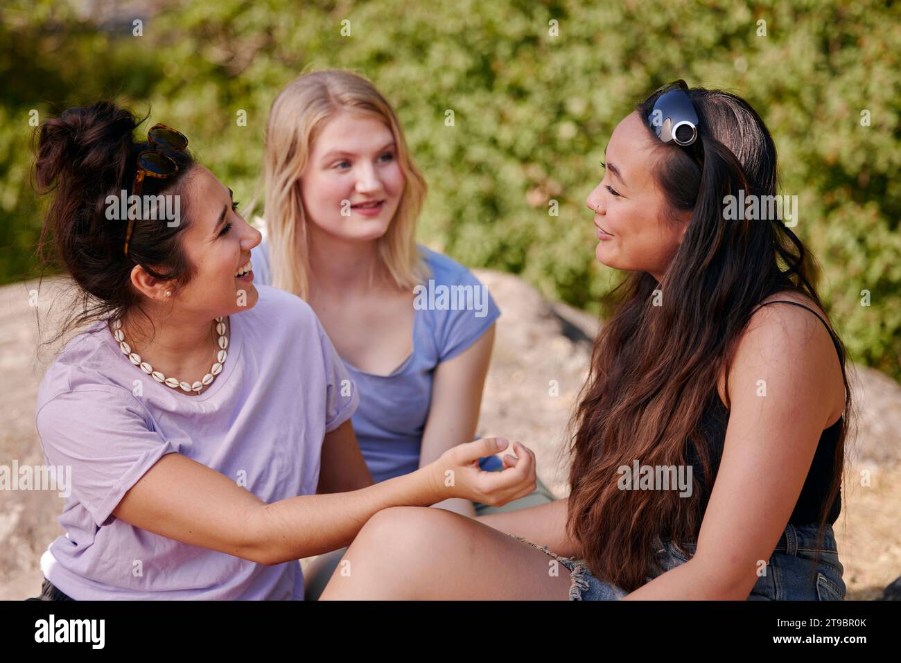 Three young female friends sitting together talking Stock Photo - Alamy