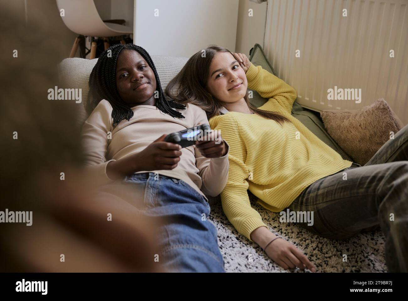 Smiling teenage girl holding game controller while lying down with ...