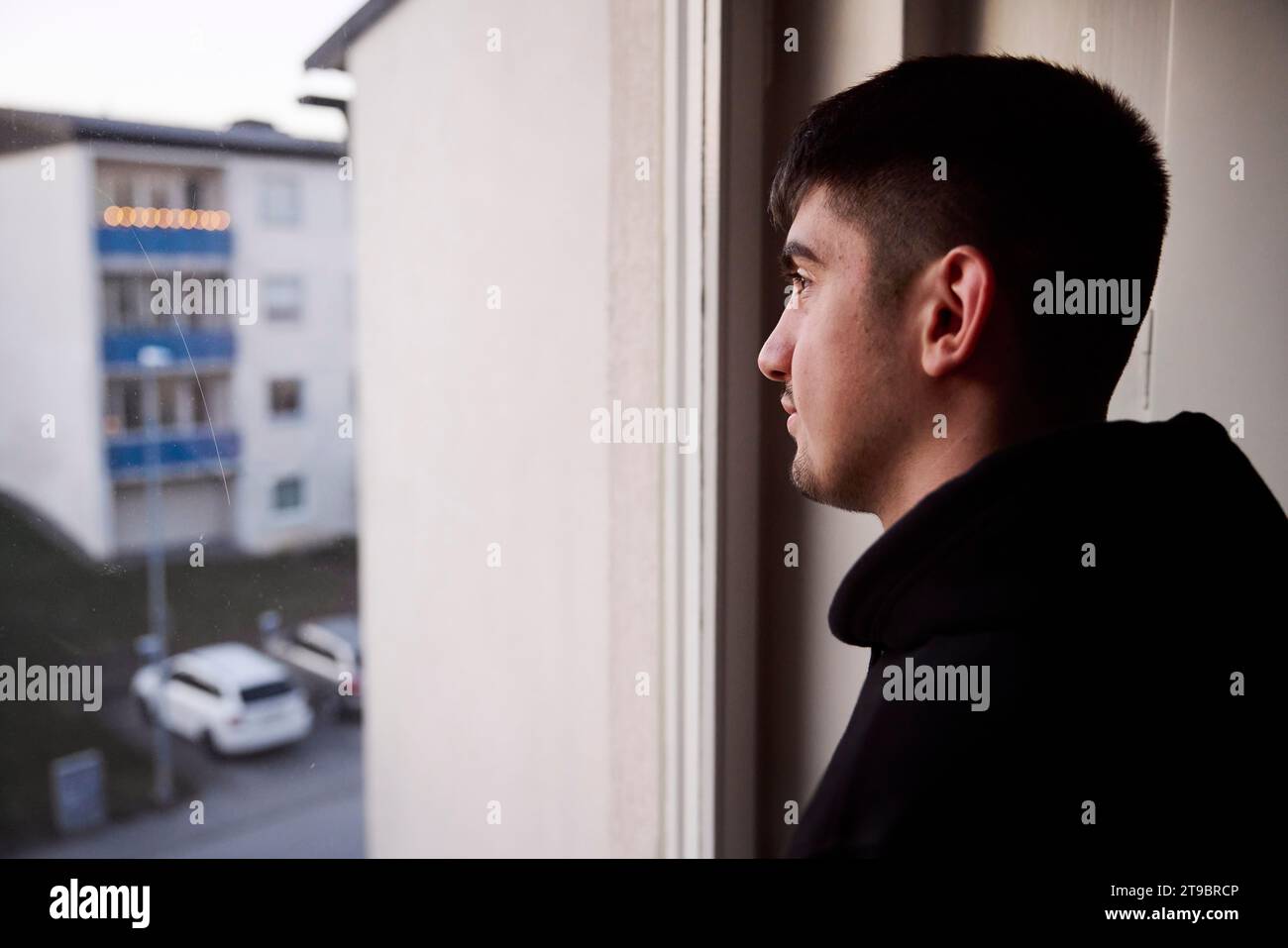 Thoughtful young man looking through window Stock Photo - Alamy