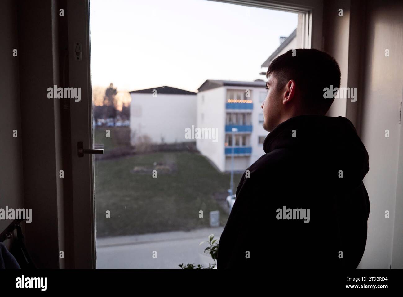 Thoughtful young man looking through window Stock Photo - Alamy