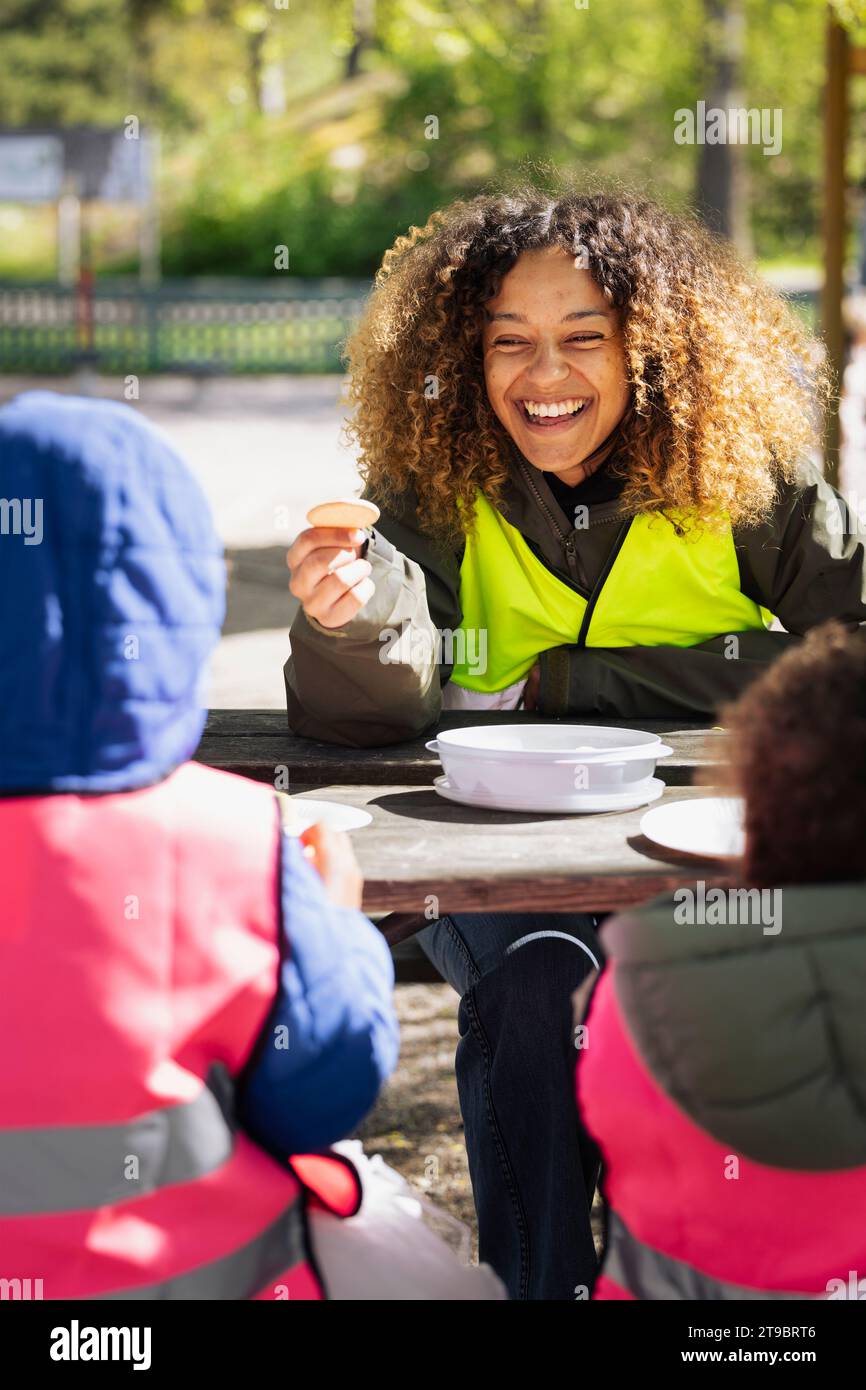 Cheerful mother giving biscuit to boy at table in park Stock Photo - Alamy