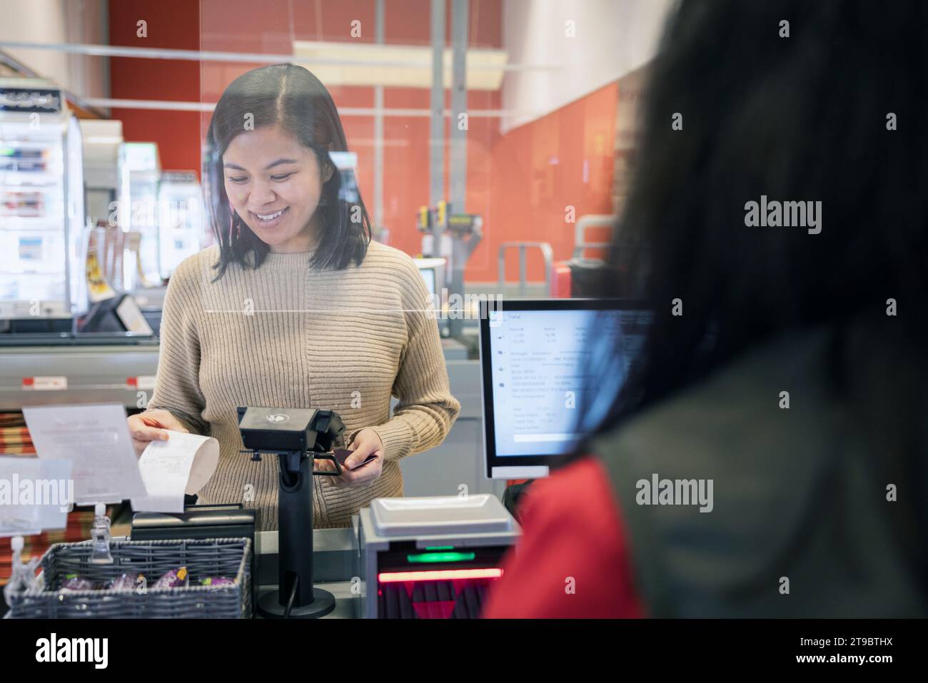 Smiling young female customer taking receipt at checkout in supermarket ...