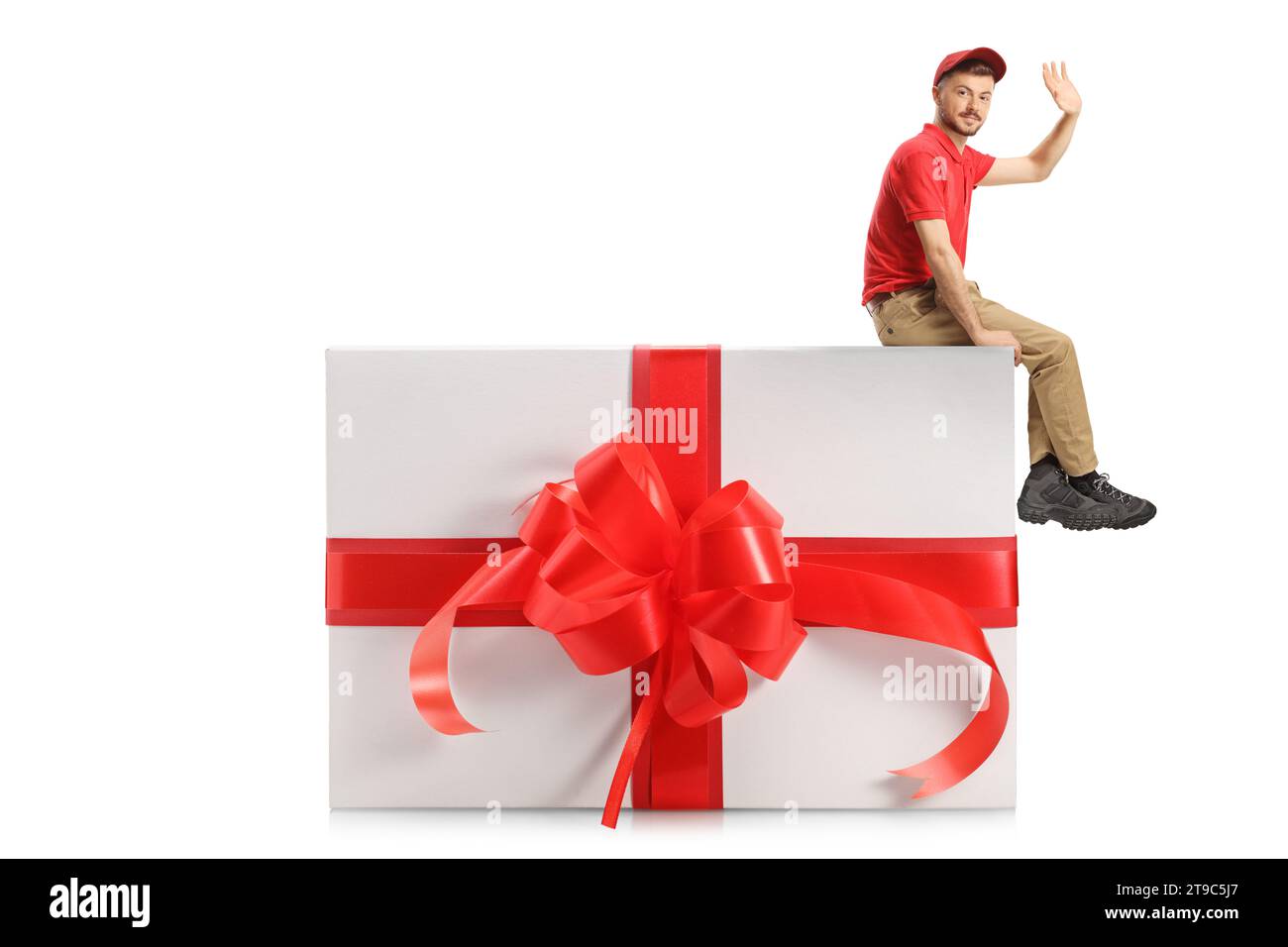 Delivery man sitting on a big present box and waving isolated on white ...