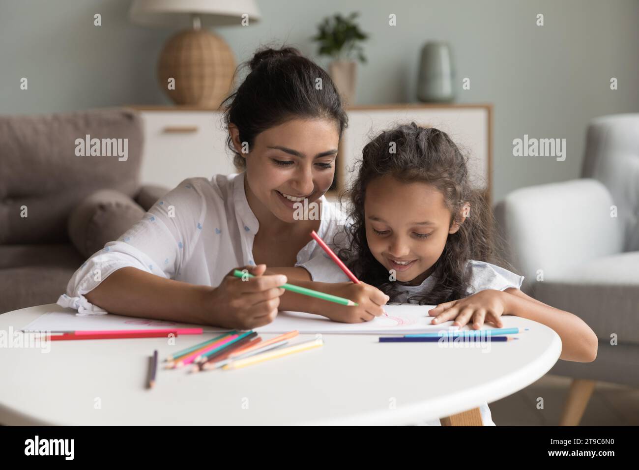 Indian mom and daughter drawing in sketchbook with colored pencils ...