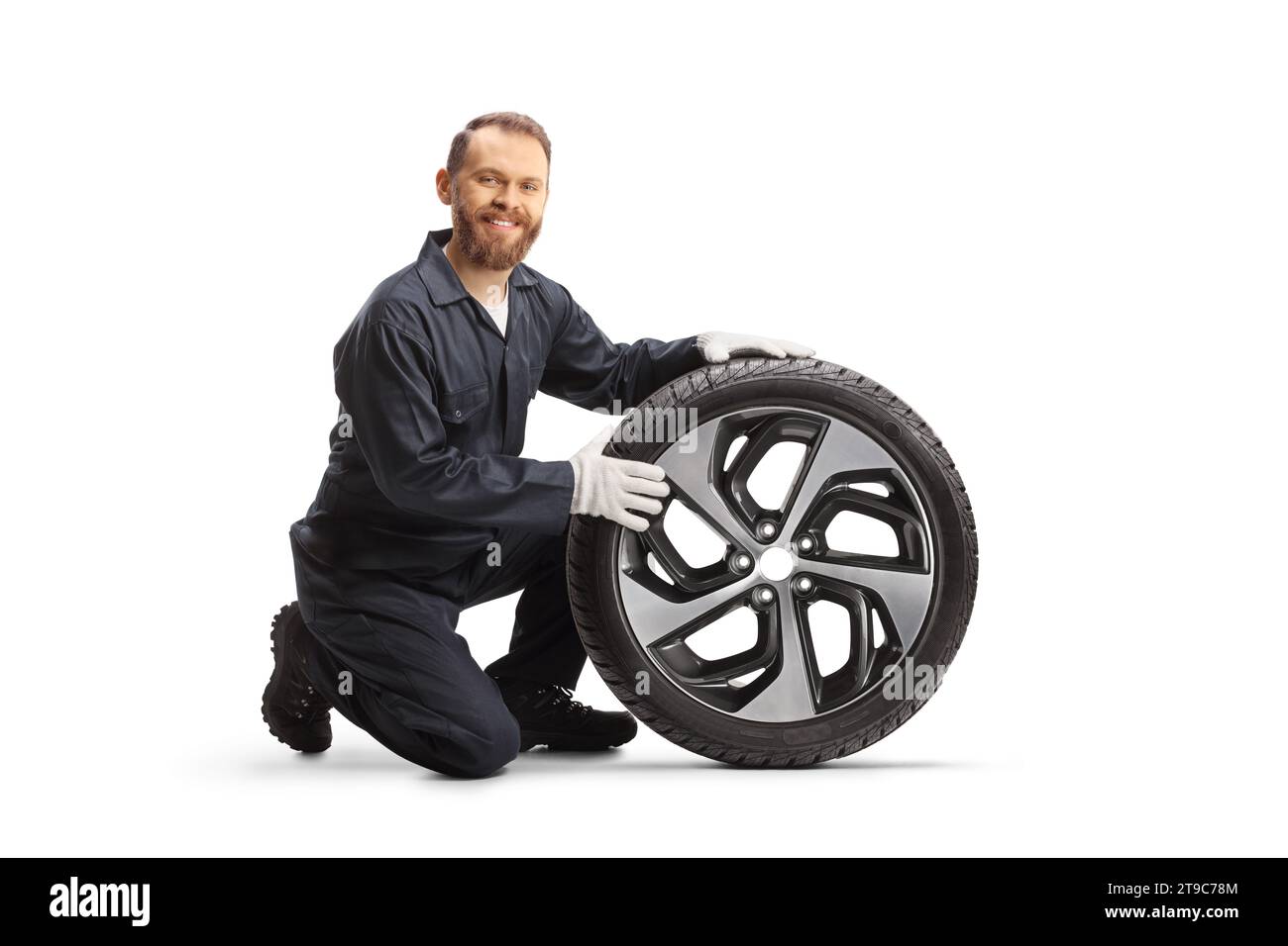 Car mechanic kneeling next to a tire with a rim and smiling isolated on ...