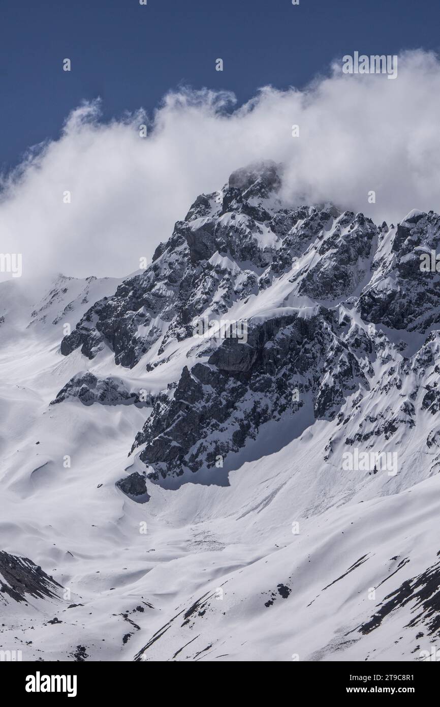 Mountain peak covered in white, fresh snow, partially veiled by fluffy ...