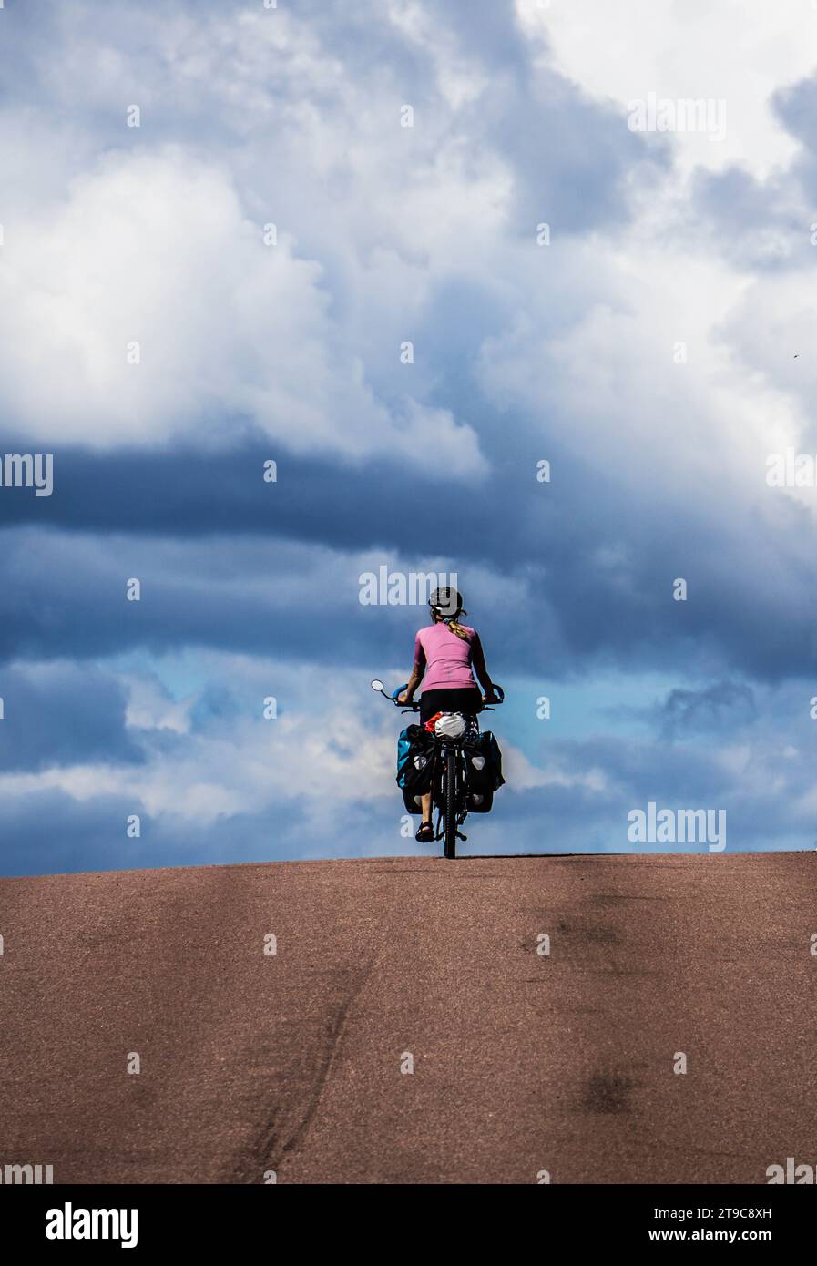 A girl on a bike is riding uphill on a red asphalt road against a ...