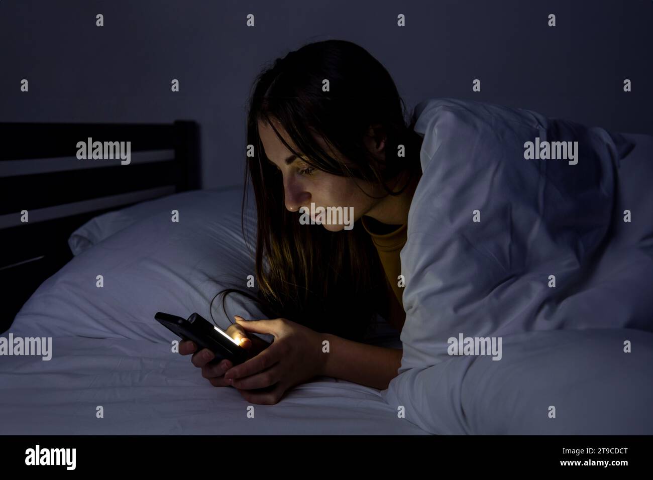 A girl in bed with a phone on a white bed in a dark room Stock Photo ...