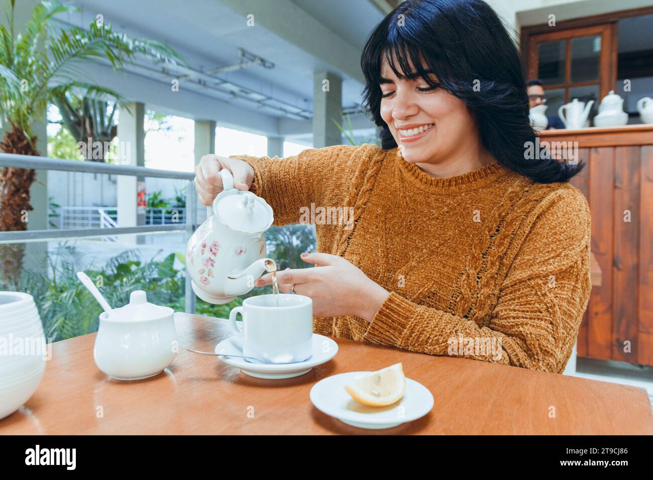 young happy latin woman is alone sitting in restaurant with teapot ...