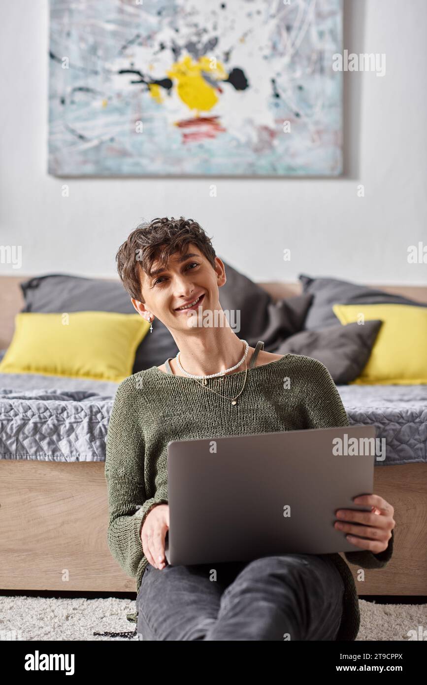 positive and curly transgender influencer using laptop and sitting next ...