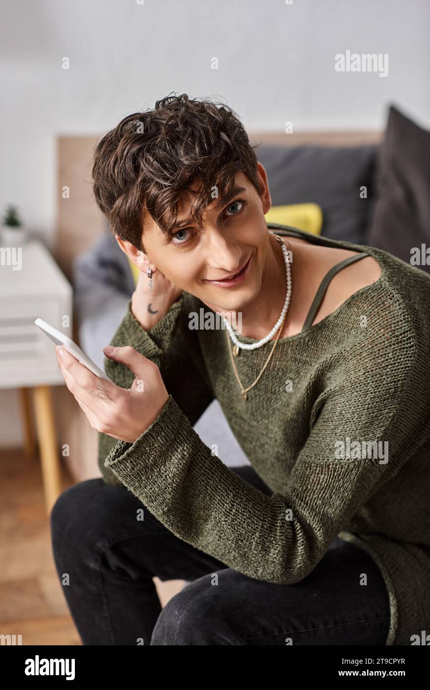 happy and curly transgender influencer using smartphone and sitting on ...