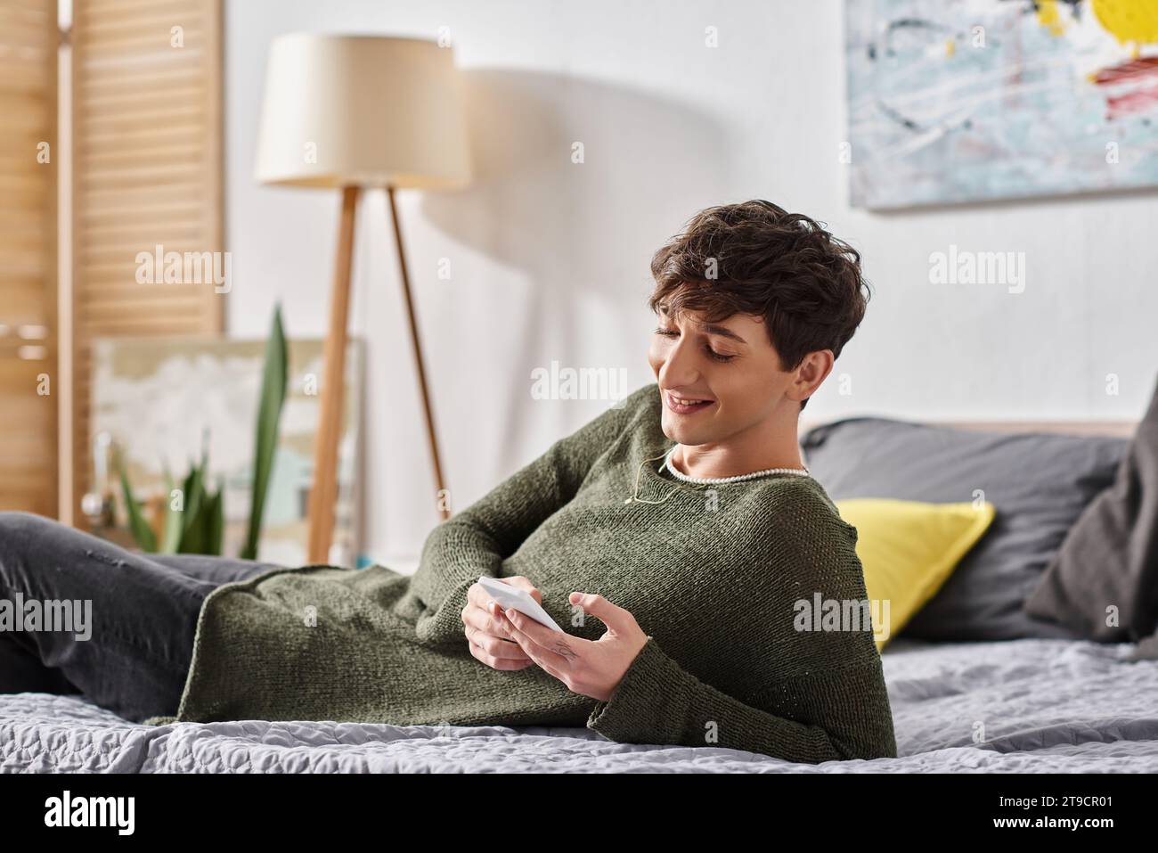 cheerful and curly transgender blogger using smartphone and lying on ...