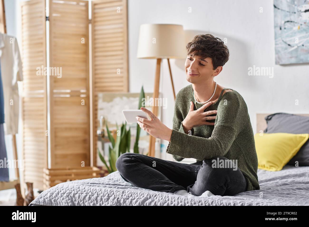 happy curly transgender influencer smiling and using smartphone while ...