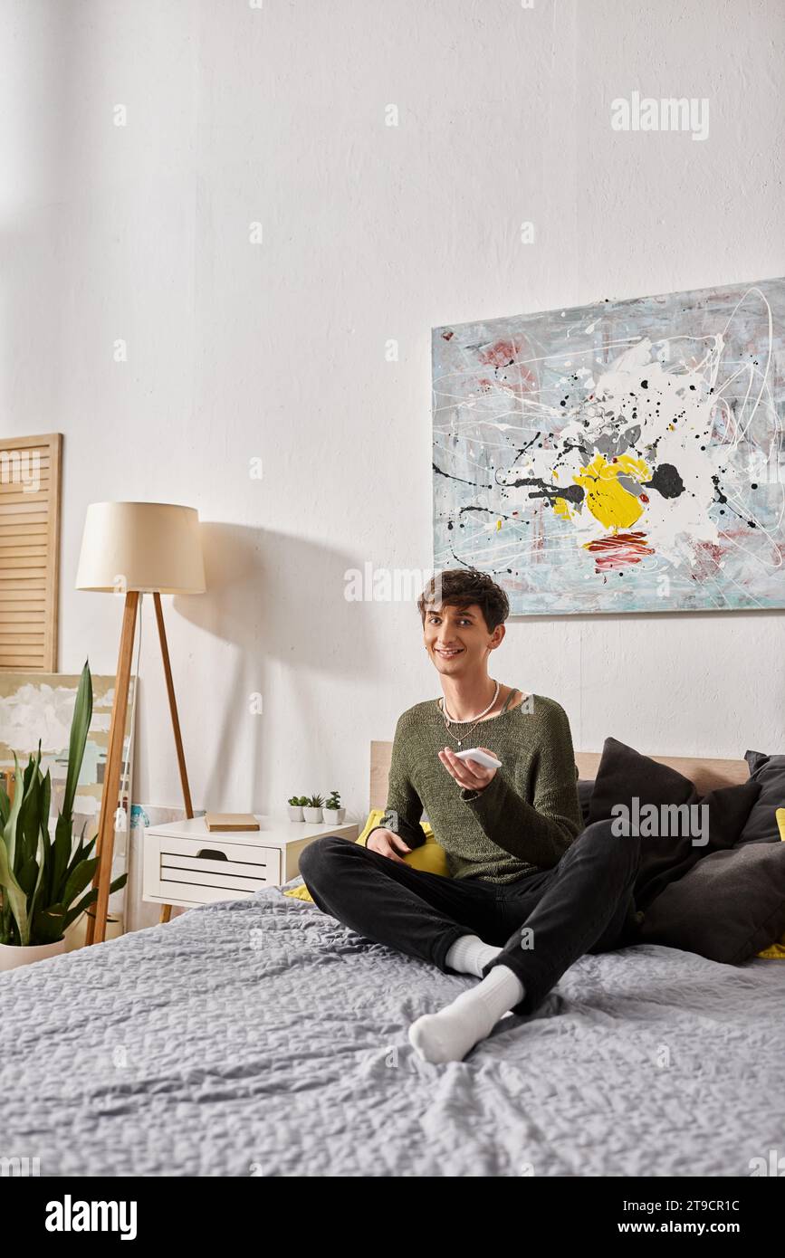 cheerful and curly transgender blogger using smartphone and sitting on ...