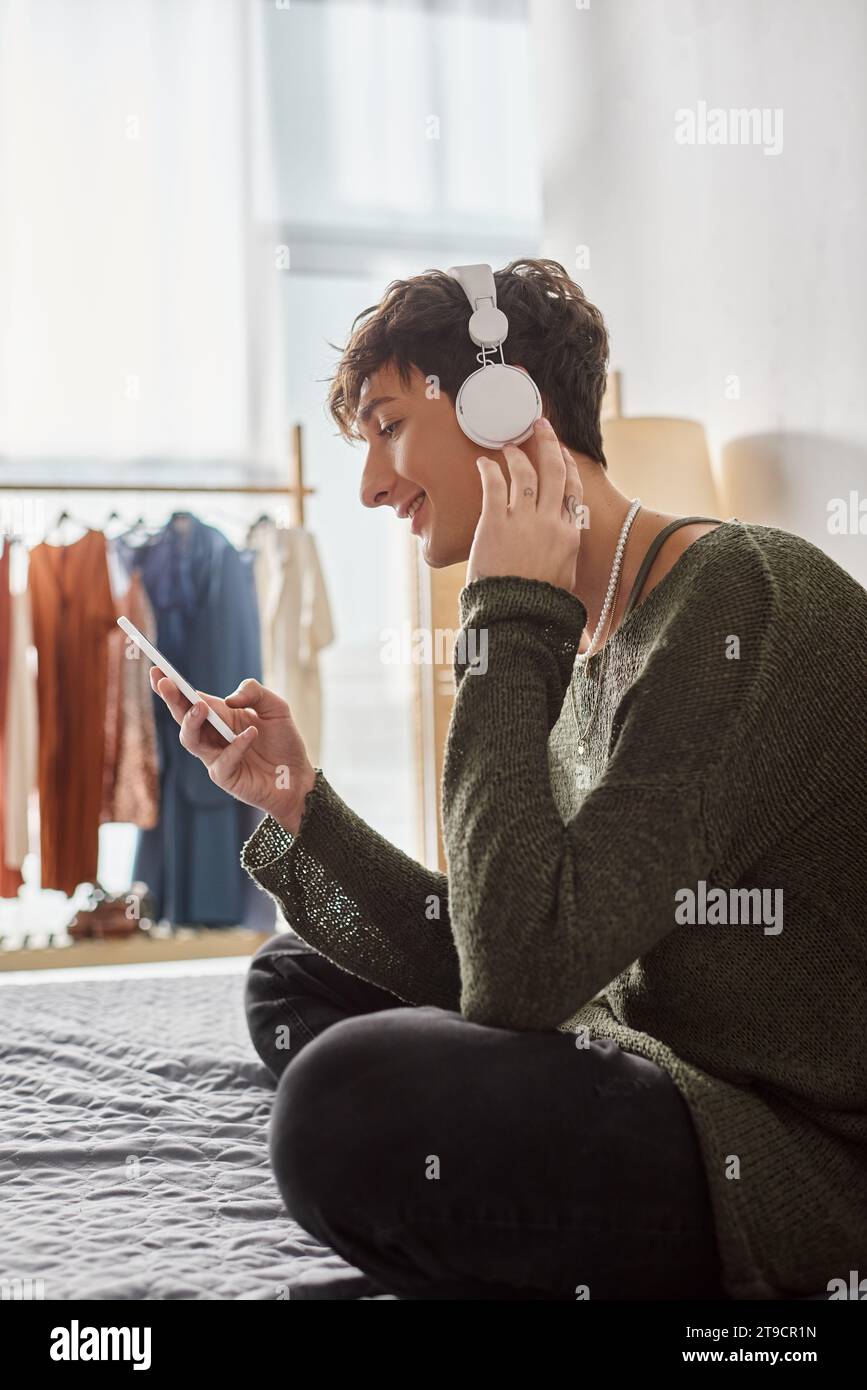 happy curly transgender person in wireless headphones holding ...