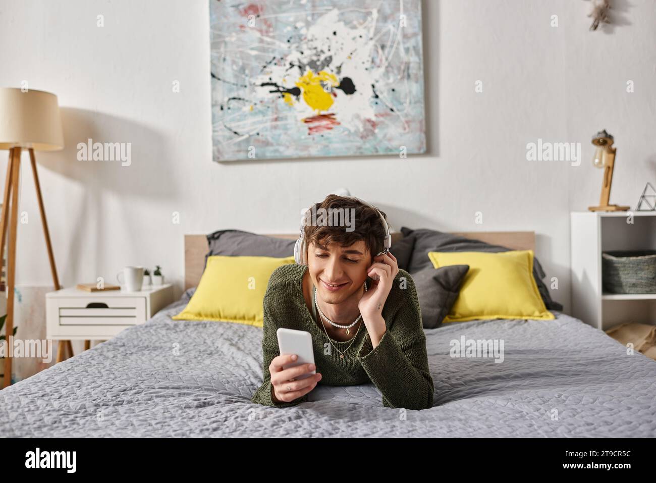 happy curly transgender person in wireless headphones holding ...