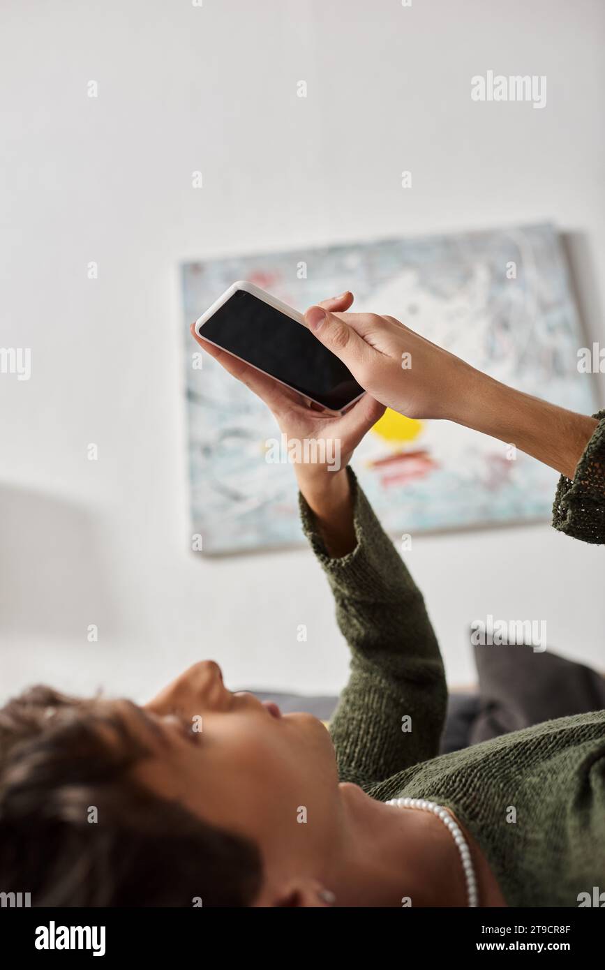 transgender blogger with curly hair using smartphone and lying on bed ...